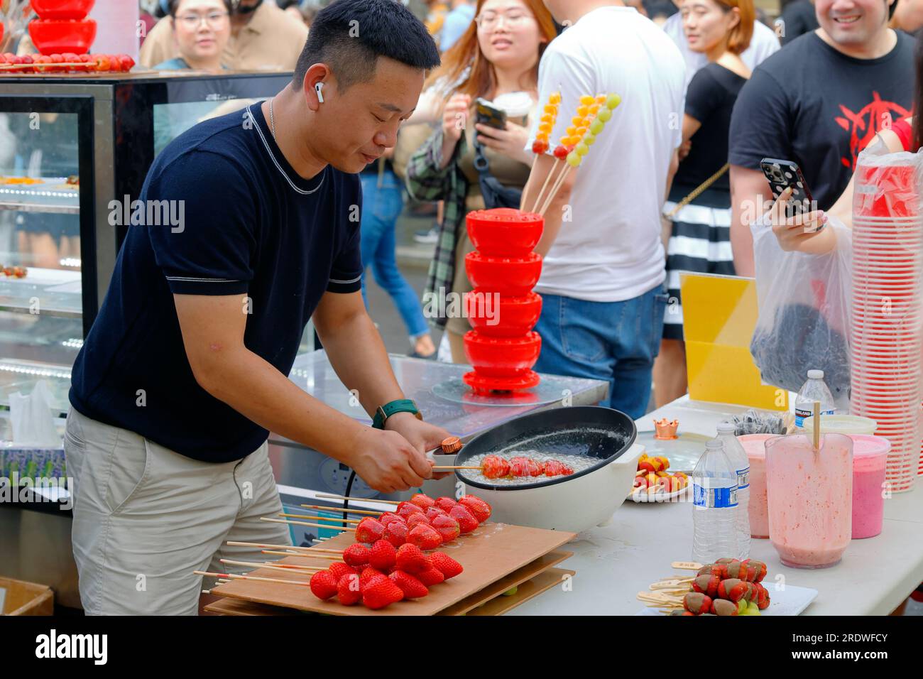 Owner of Chan Bai Mei candy shop making candied strawberries on a stick ...