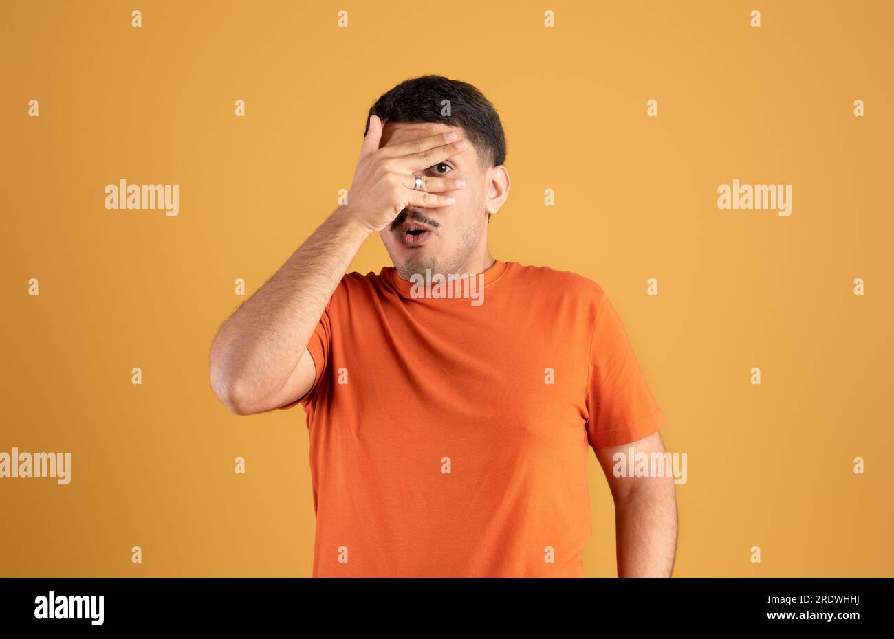 Shocked brazilian man closing his face with palms, looking with one eye ...
