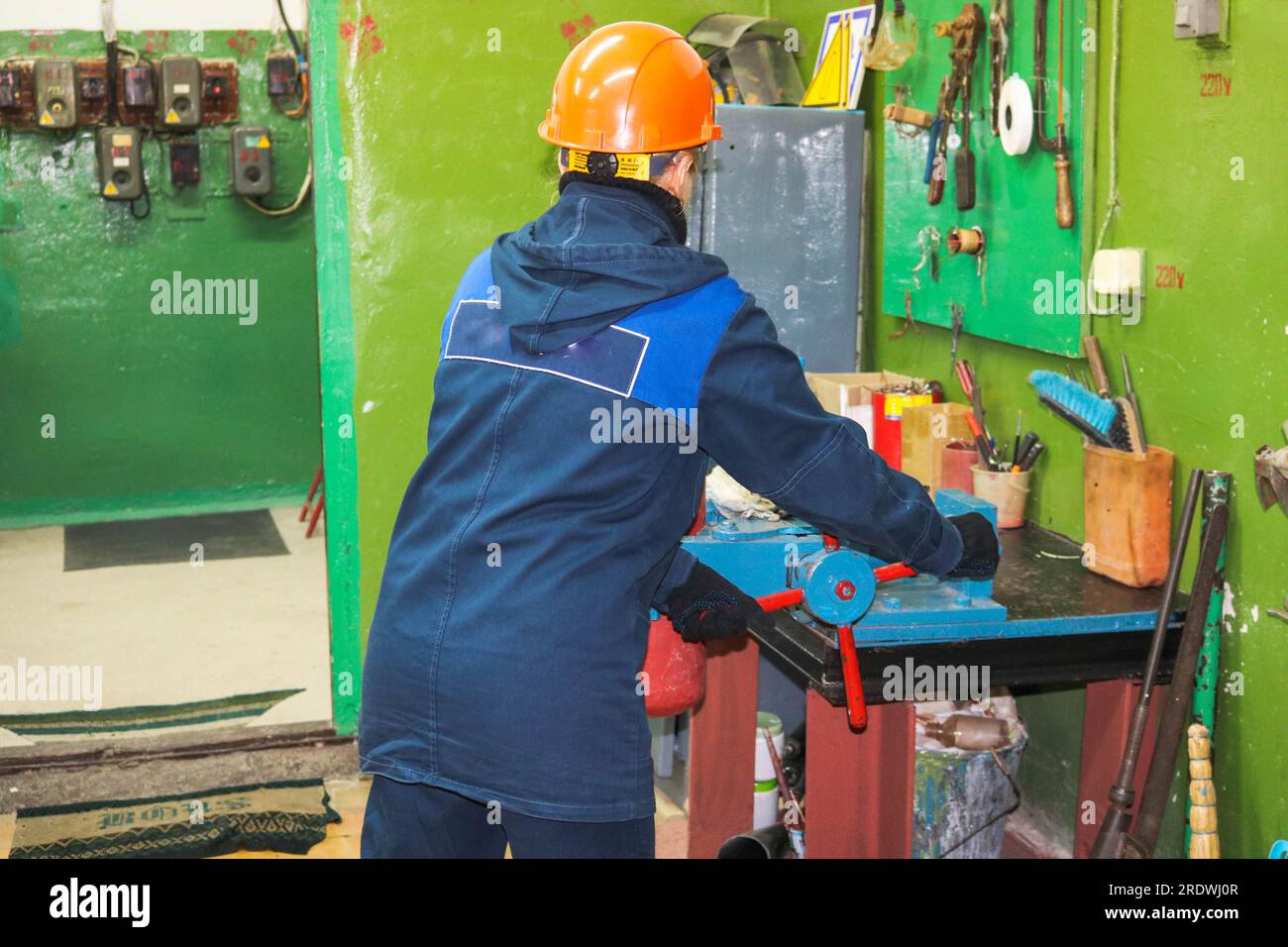 A male worker on a large metal industrial vice is repairing a red fire ...