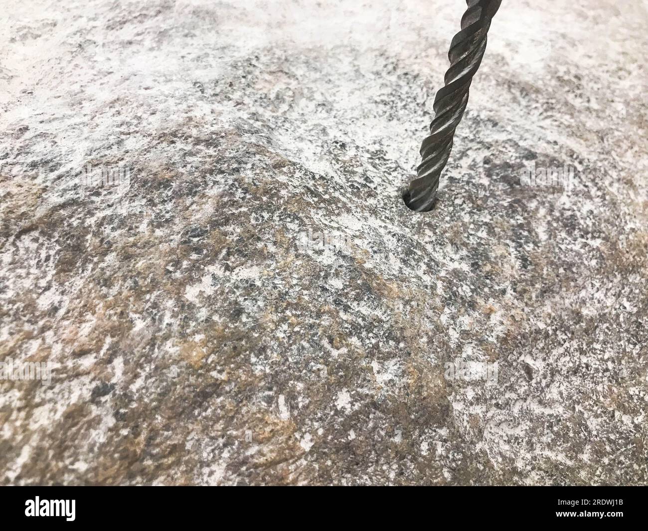 A sturdy, hard metal iron drill bit drills a hole in a large gray stone ...