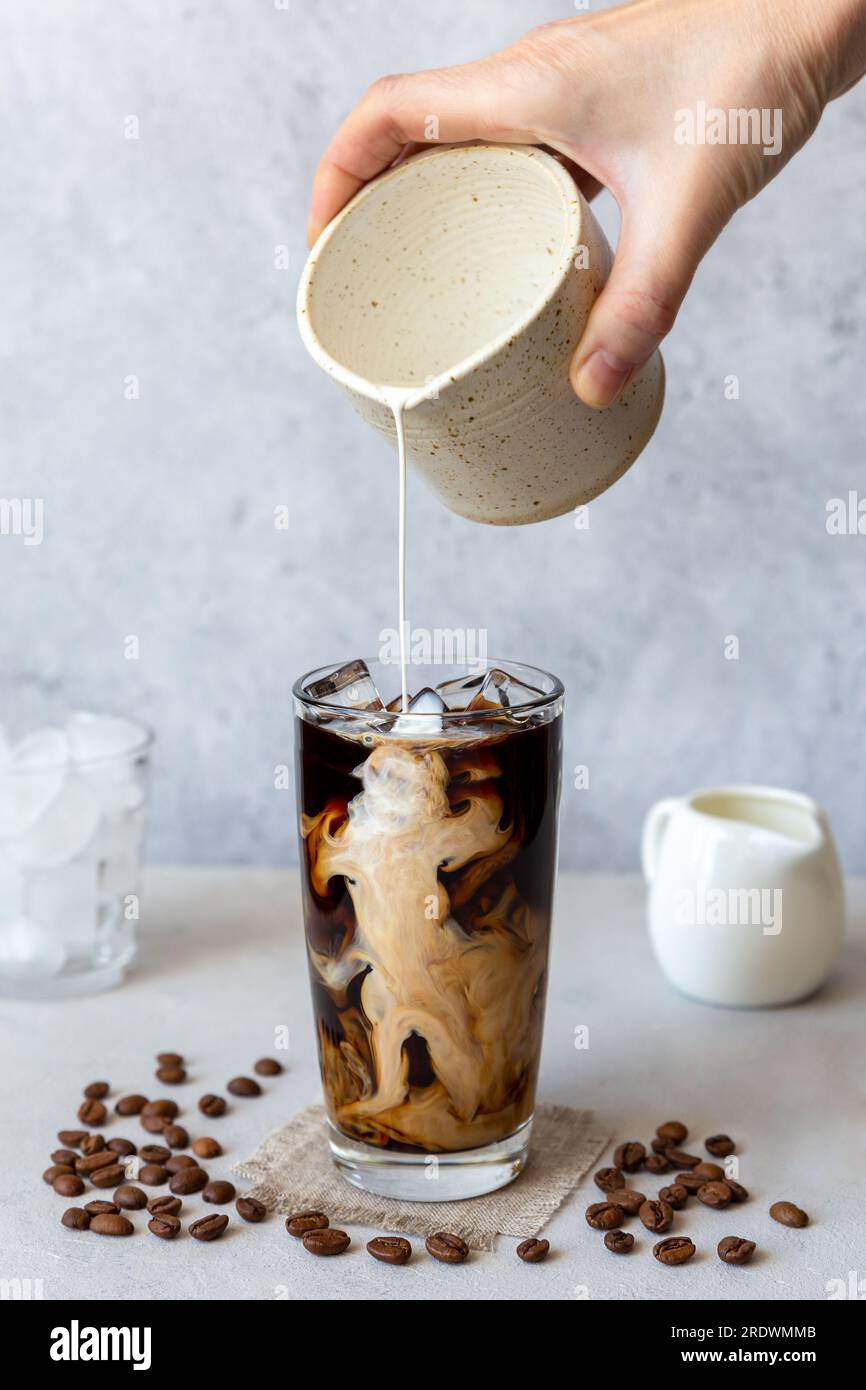 Iced coffee in a tall glass with cream pouring from the top, a glass ...