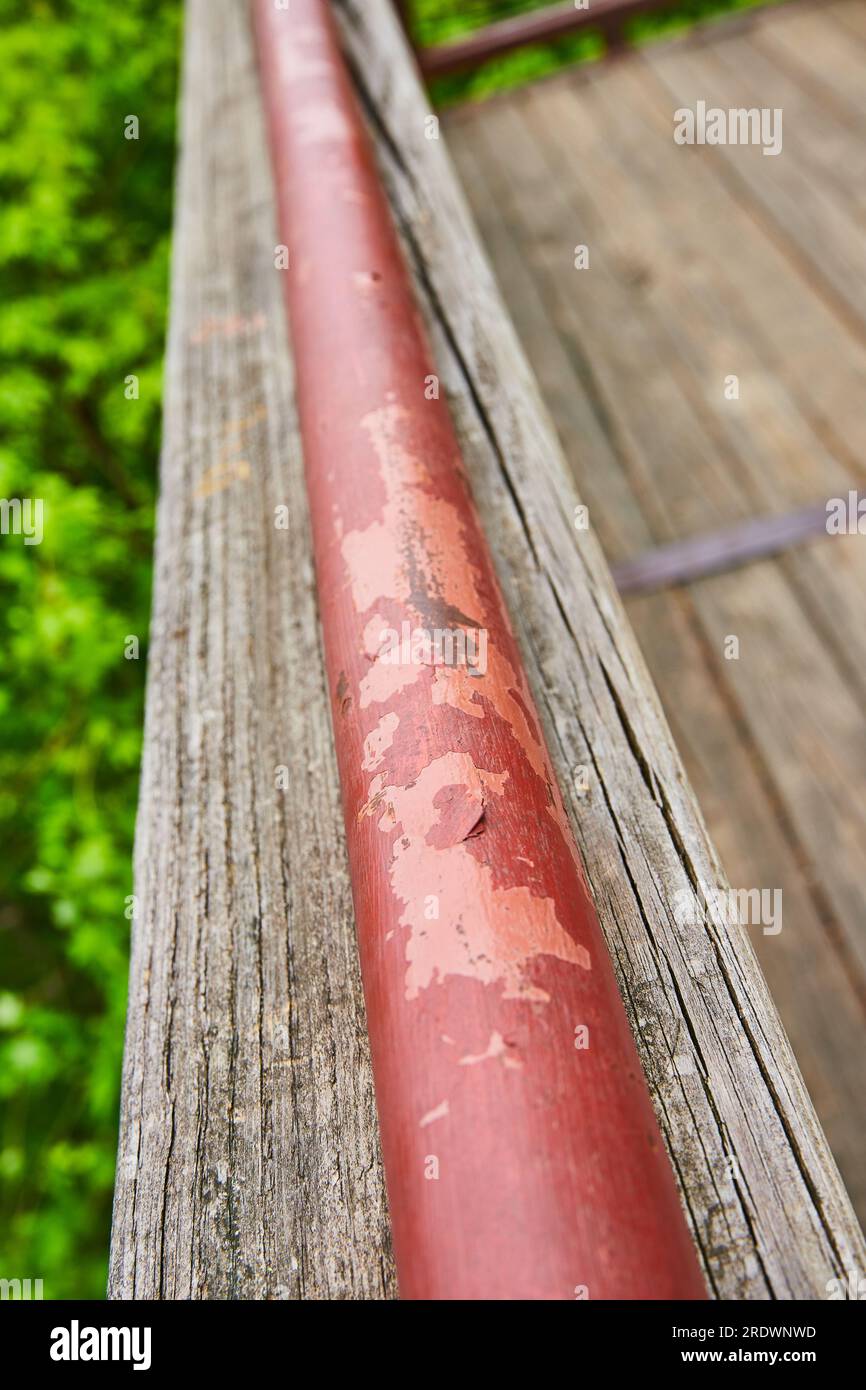 Long chipped red painted metal railing on top of weather worn wood beam ...