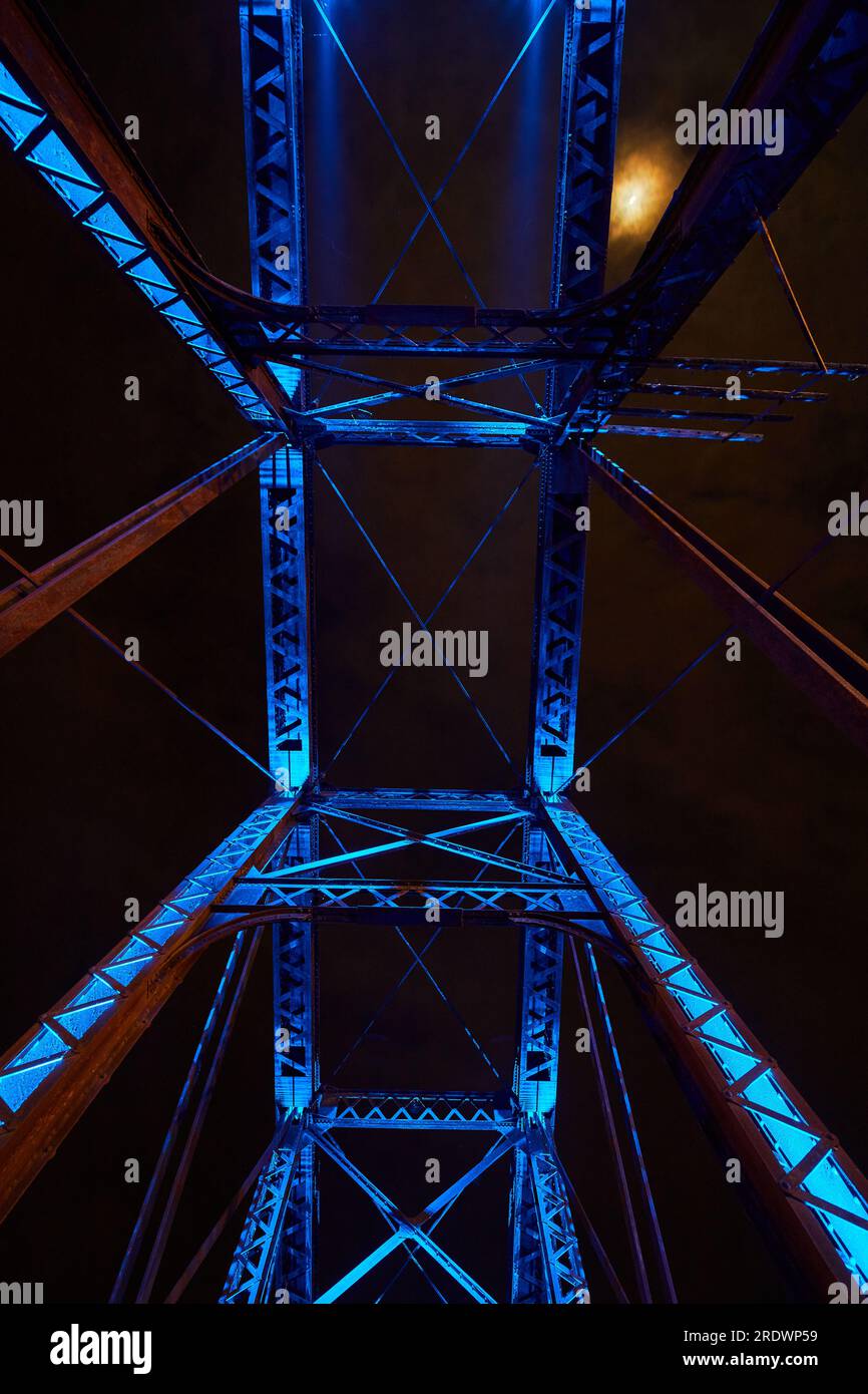 Upward view of truss railroad bridge beams lit in neon blue light at ...