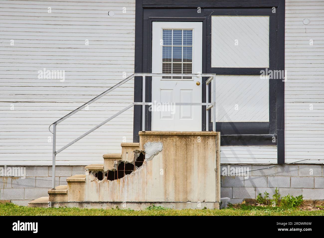 House with white siding and door with black frames and busted concrete ...