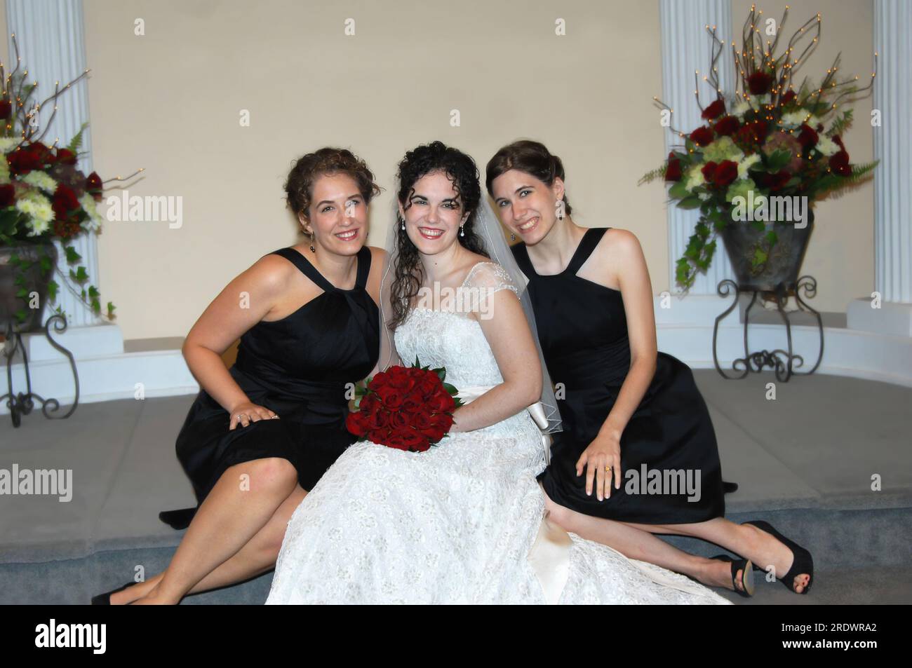 Bride and her two sisters sit on the steps of the wedding chapel. Two ...