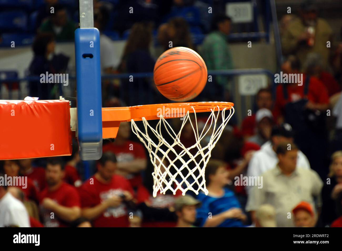 Crowded gymnasium watches a spinning basketball drop into the orange ...