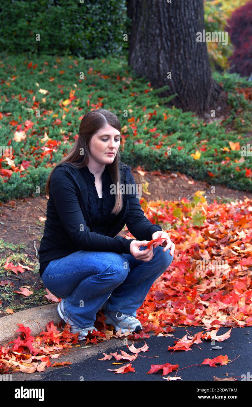 Young woman sits on curb in downtown Asheville, North Carolina. She is ...