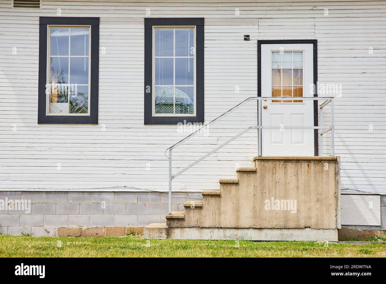 Common whit house with white door and concrete steps and items crowding ...