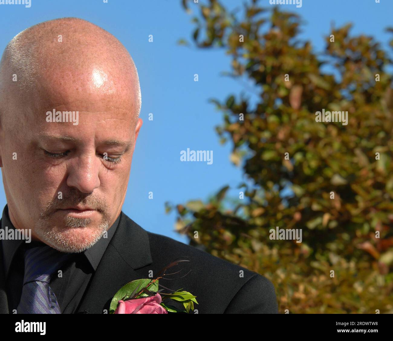 During outdoor wedding ceremony, the groom bows his head to pray. Sky ...