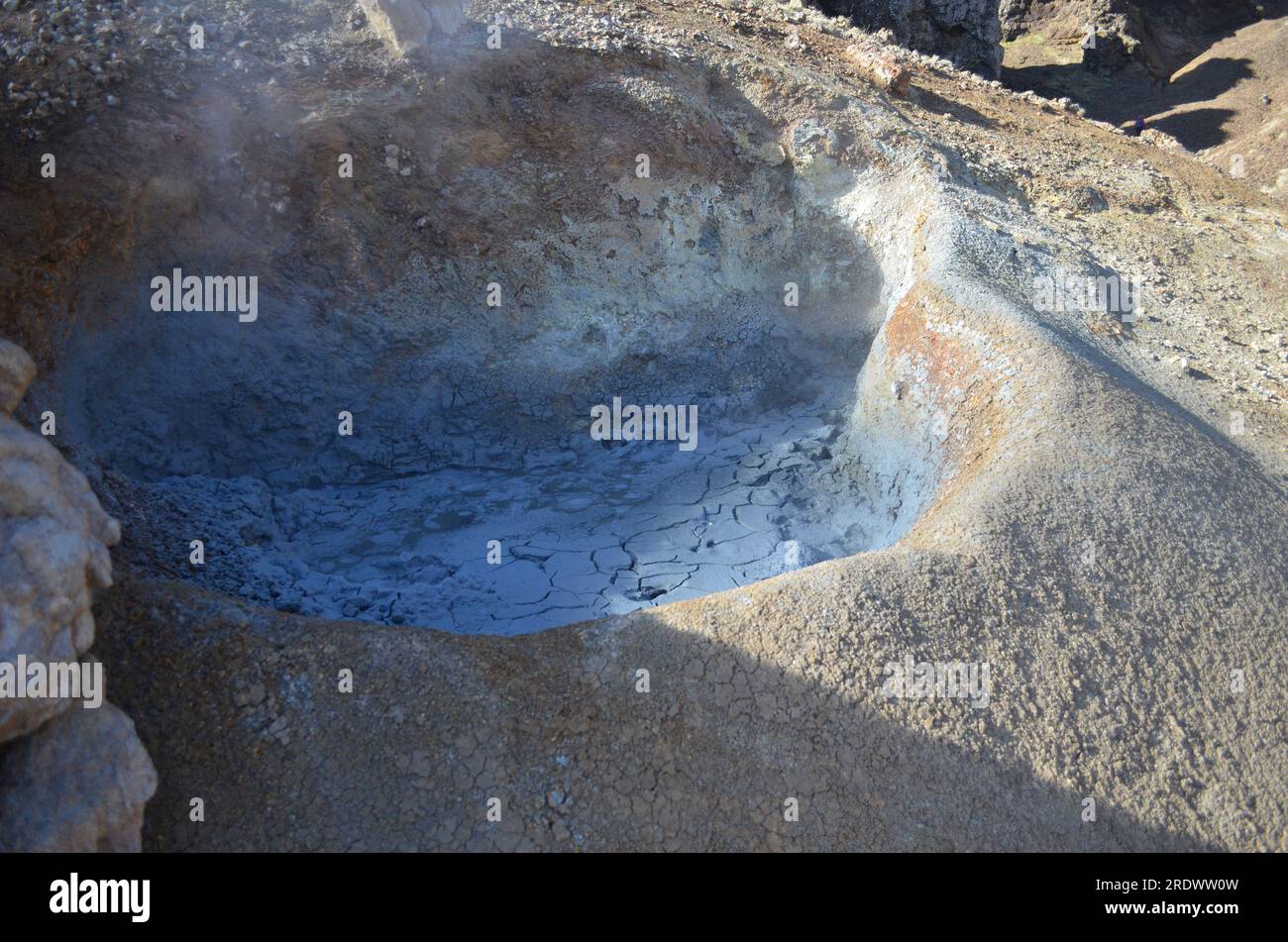 Dried cracking mud in a old fumarole hole with steam rising in southern ...