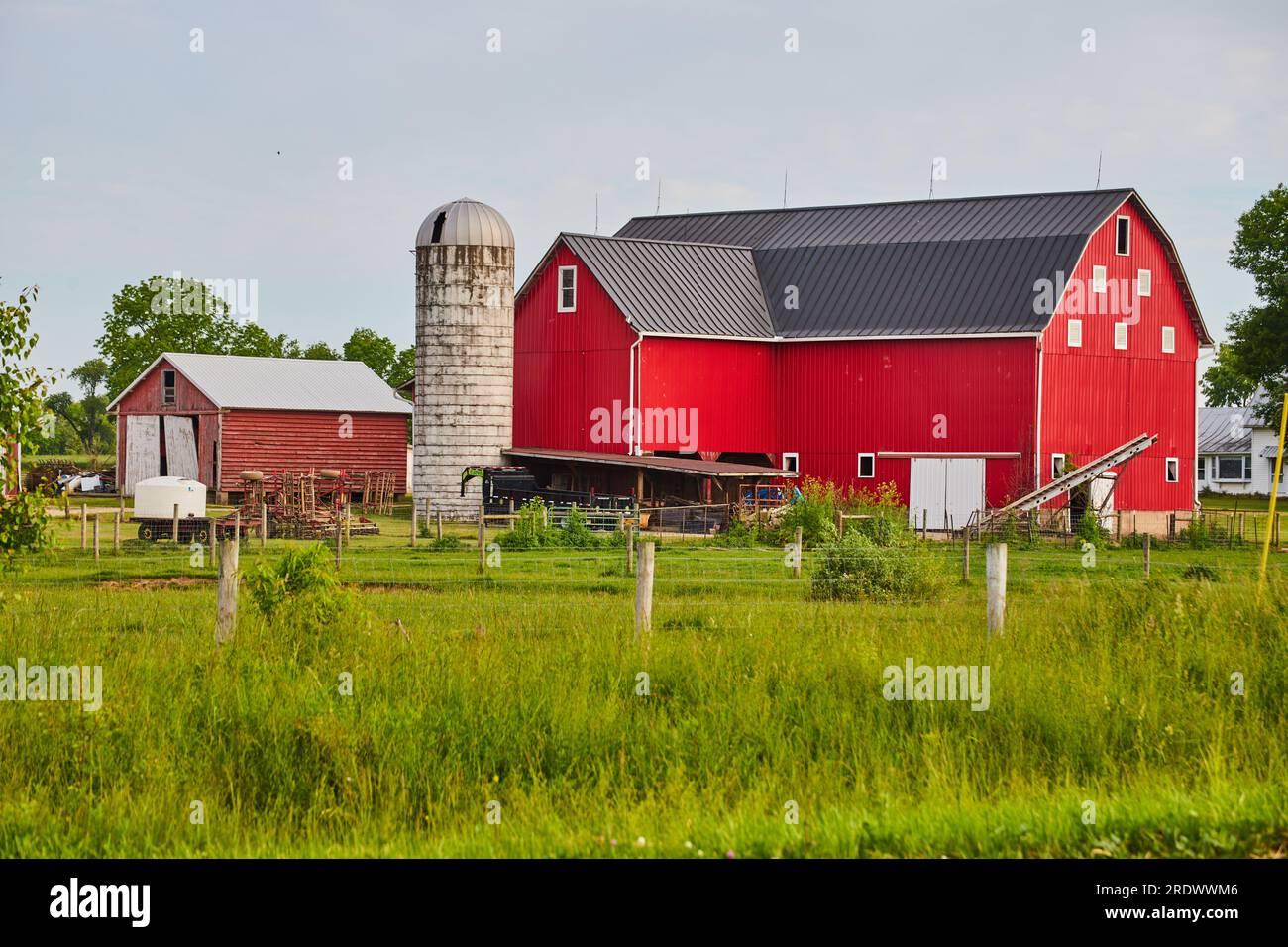 Red barn and dirty white silo on farm with wood poles and wire fencing ...