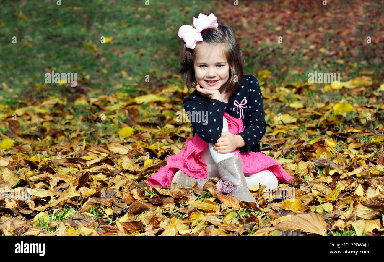 Impish little girl pauses to smile while playing in the leaves on an ...
