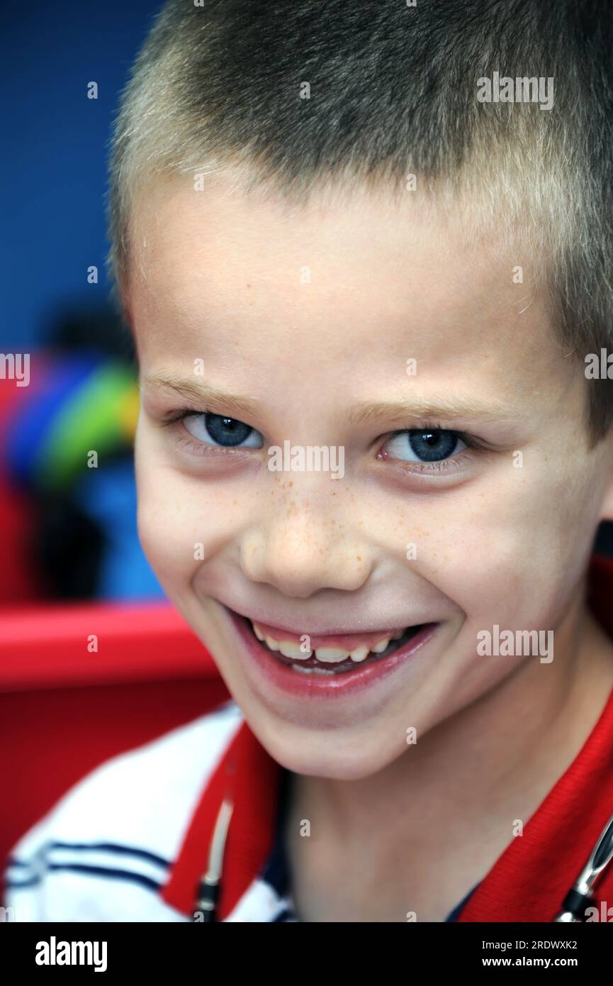 Little boy smiles sheepishly for the camera. Closeup shows his freckles ...