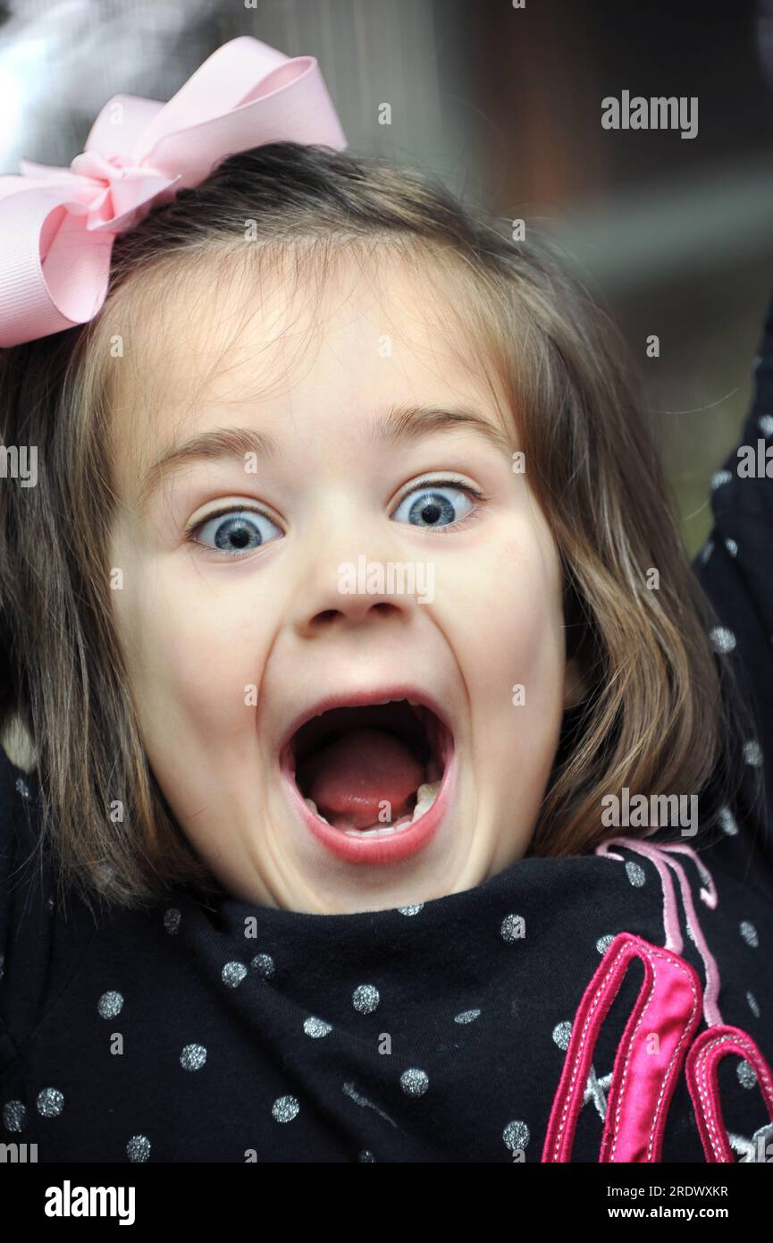 Little girl screams for joy in a closeup photo. She is wearing a pink ...