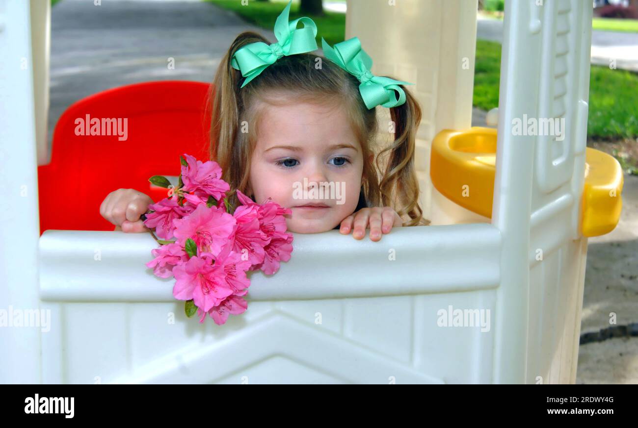 Little girl hangs dejectedly on the window of her playhouse. She is ...