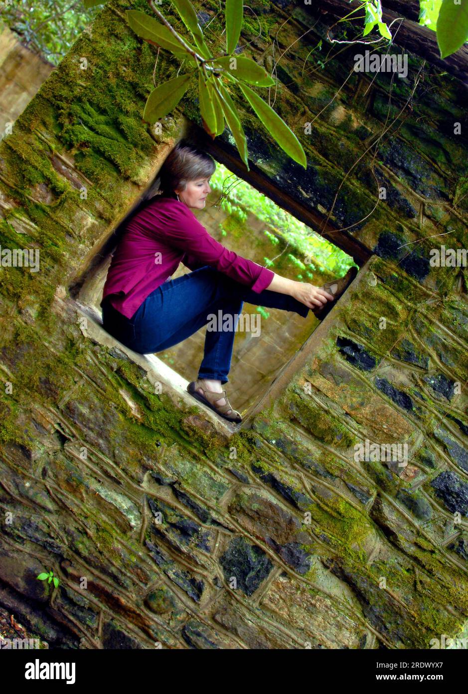 Woman crouches in a moss covered window, in a forgotten stone building ...