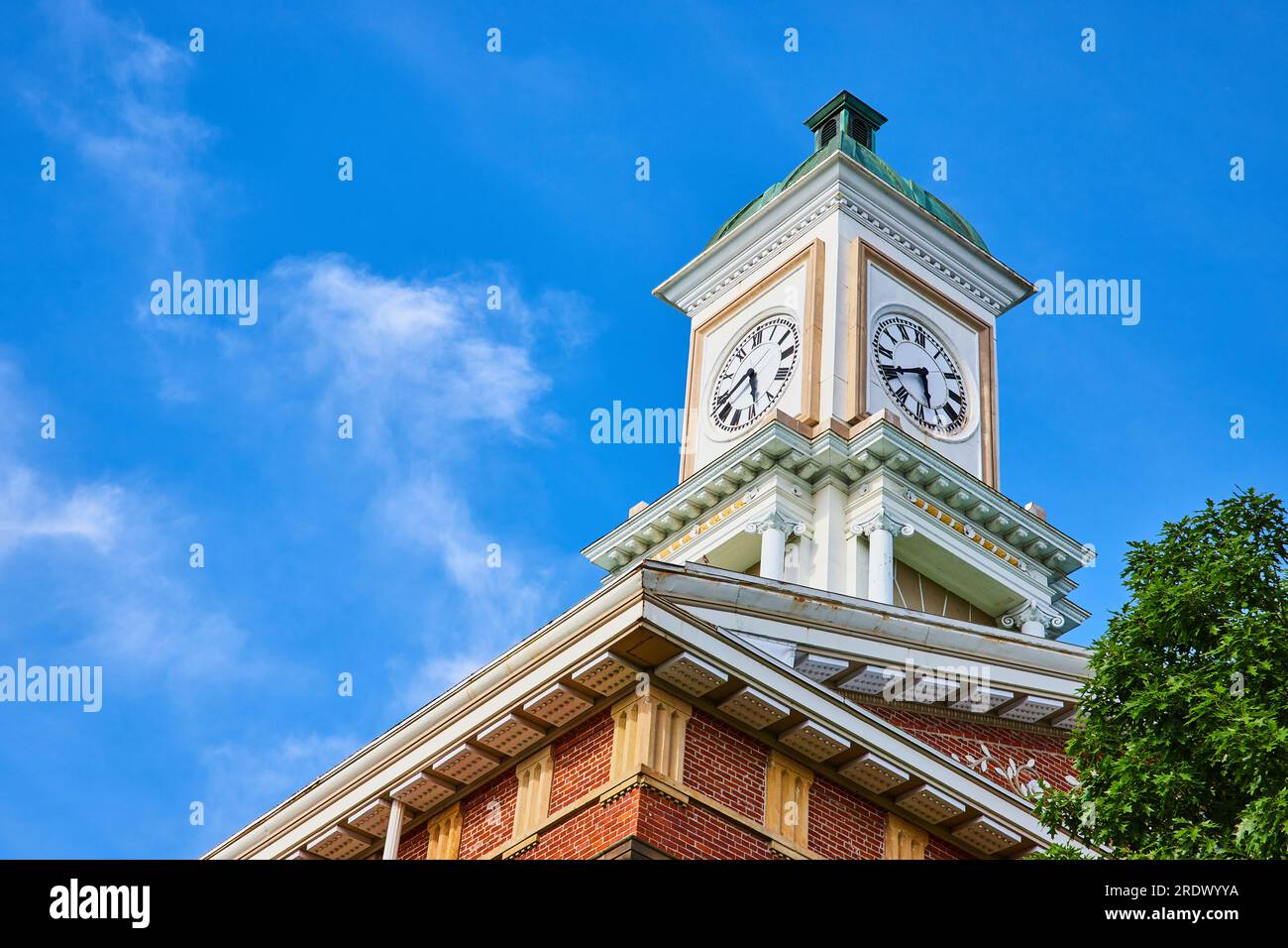 Clock tower on brick building roof with blue skies and green tree top ...