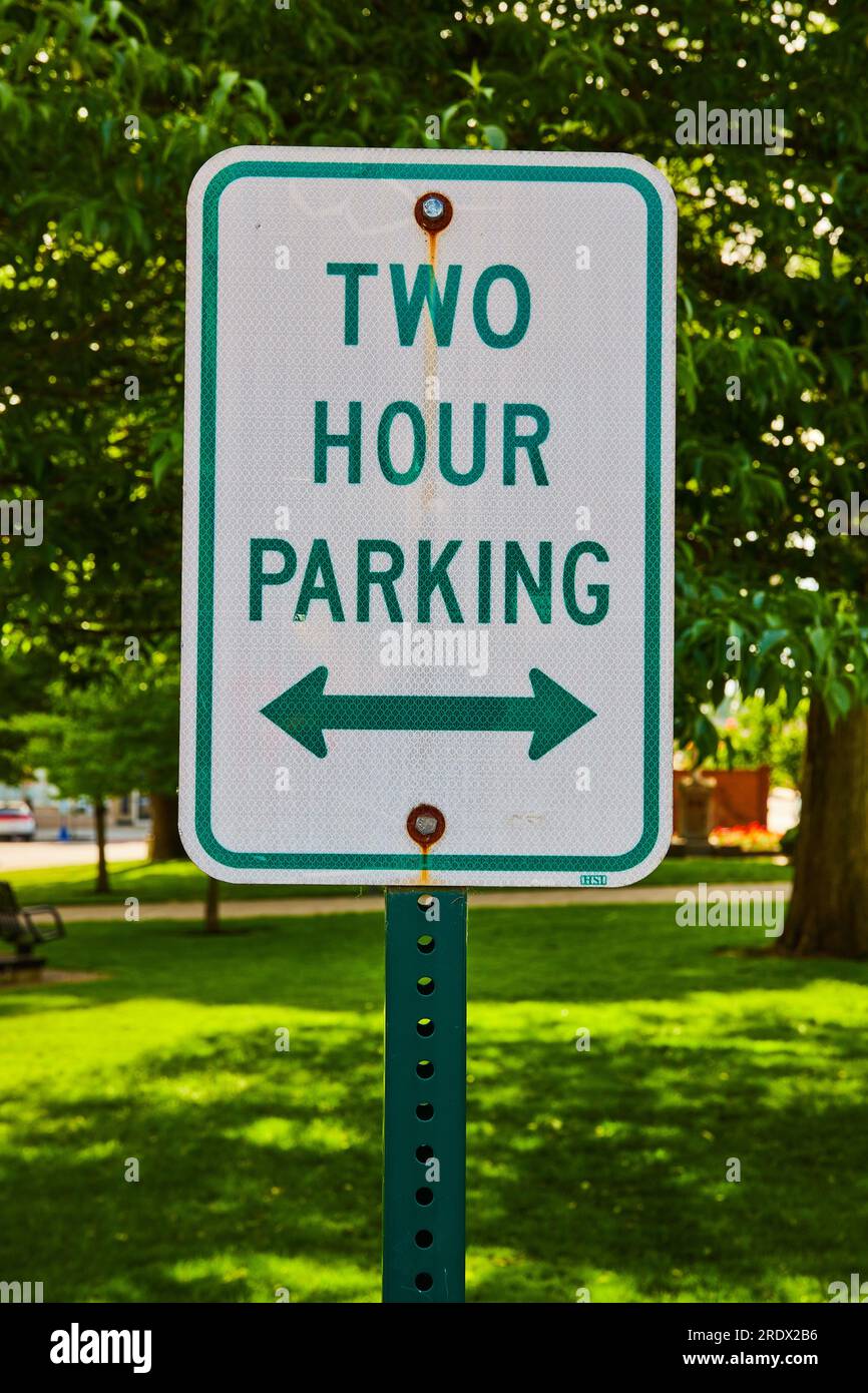 Vertical of tall green Two Hour Parking sign with green lawn and trees ...