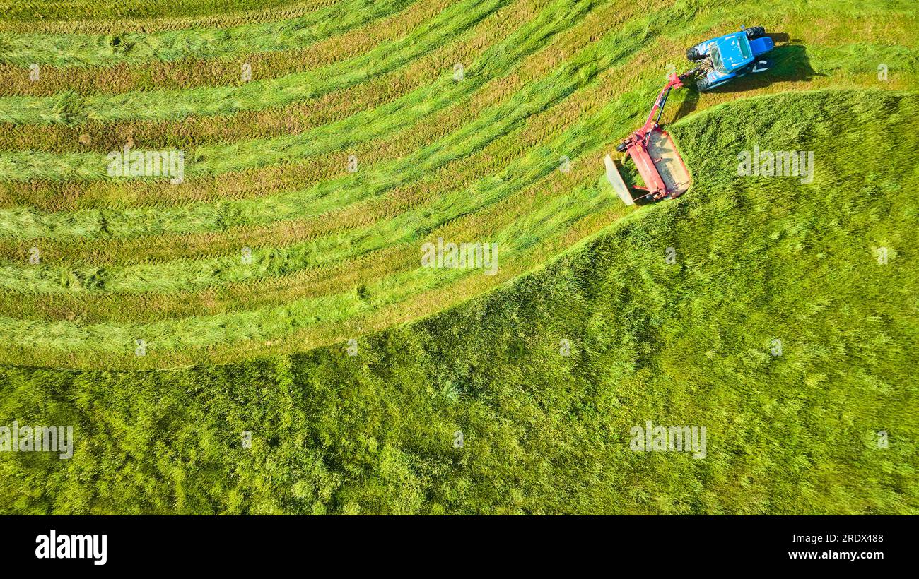 Background asset aerial of blue tractor pulling mower in curved wave ...
