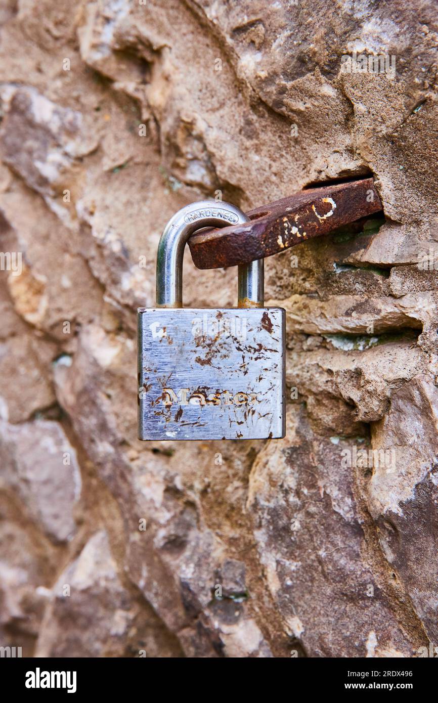 Tan rock wall, rusty metal loop, hook, rusting closed silver metal lock ...