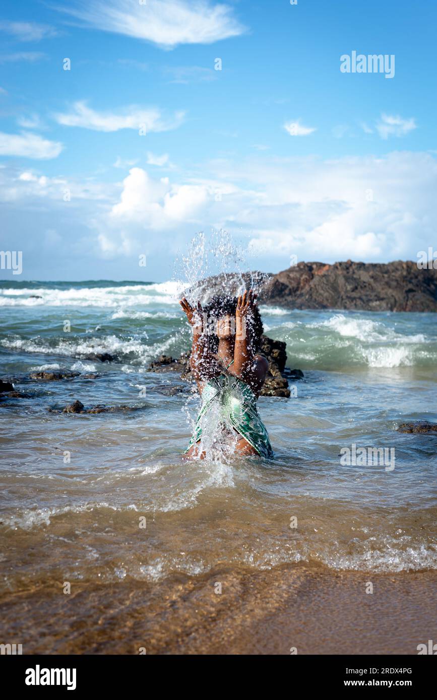 Portrait of beautiful woman with black power hair kneeling on beach ...