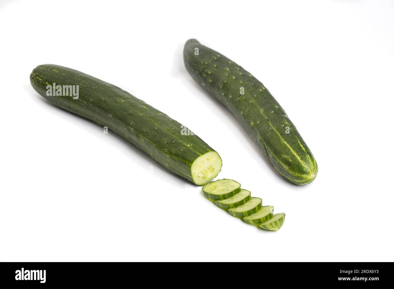 A close up photo of whole and partially sliced cucumbers set on a white ...