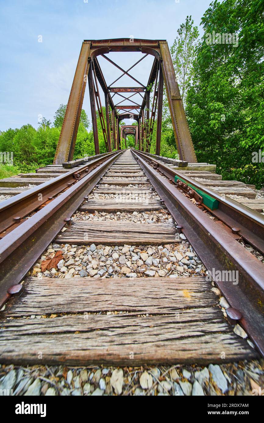 Low view of railroad tracks as they cross over train bridge to green ...