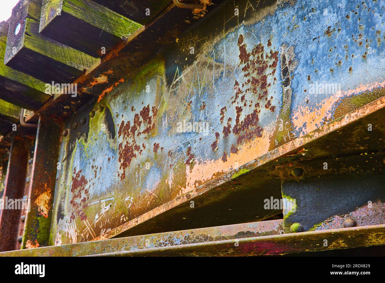 Blue and yellow rust corrosion on underside of railroad train bridge with wood beams from tracks ...