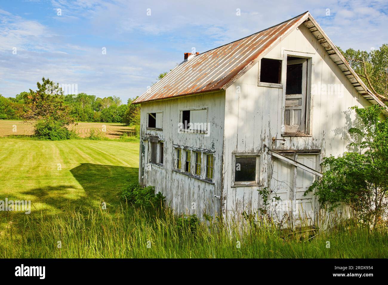 Abandoned farm house in grassy field near farmland with busted windows ...