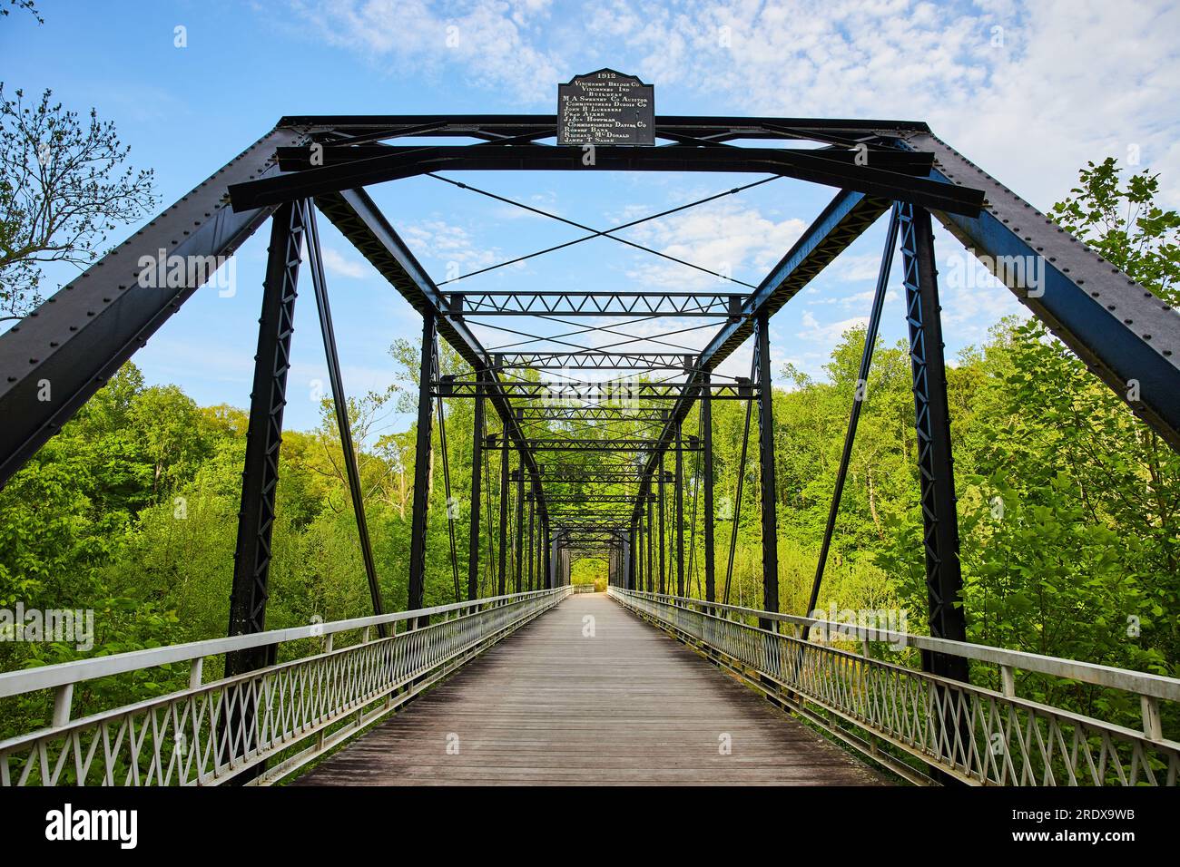 Lush, green forest wall behind large dark metal bridge, black beams ...