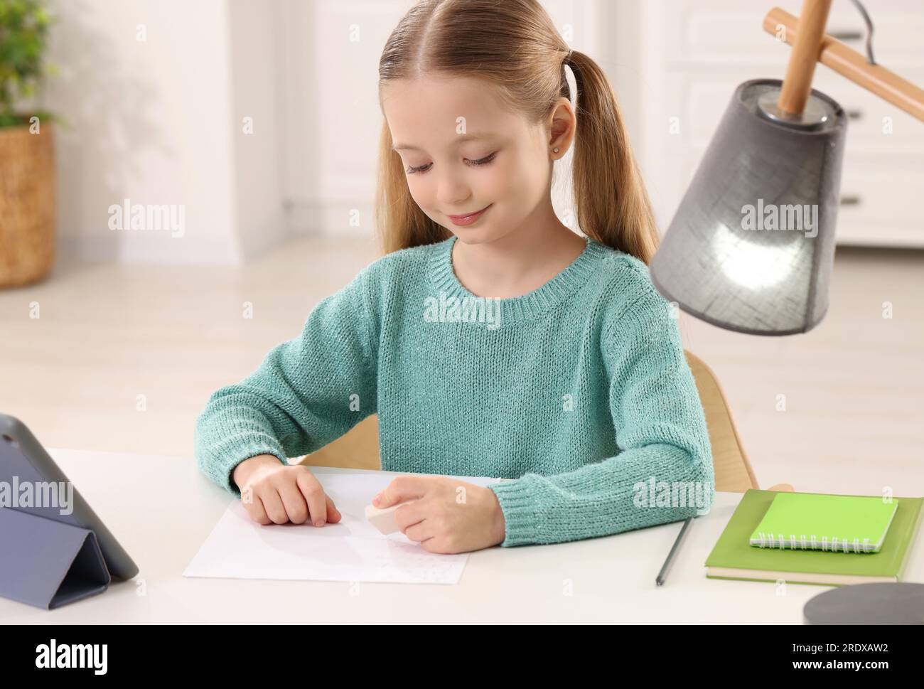 Girl using eraser at white desk in room Stock Photo - Alamy