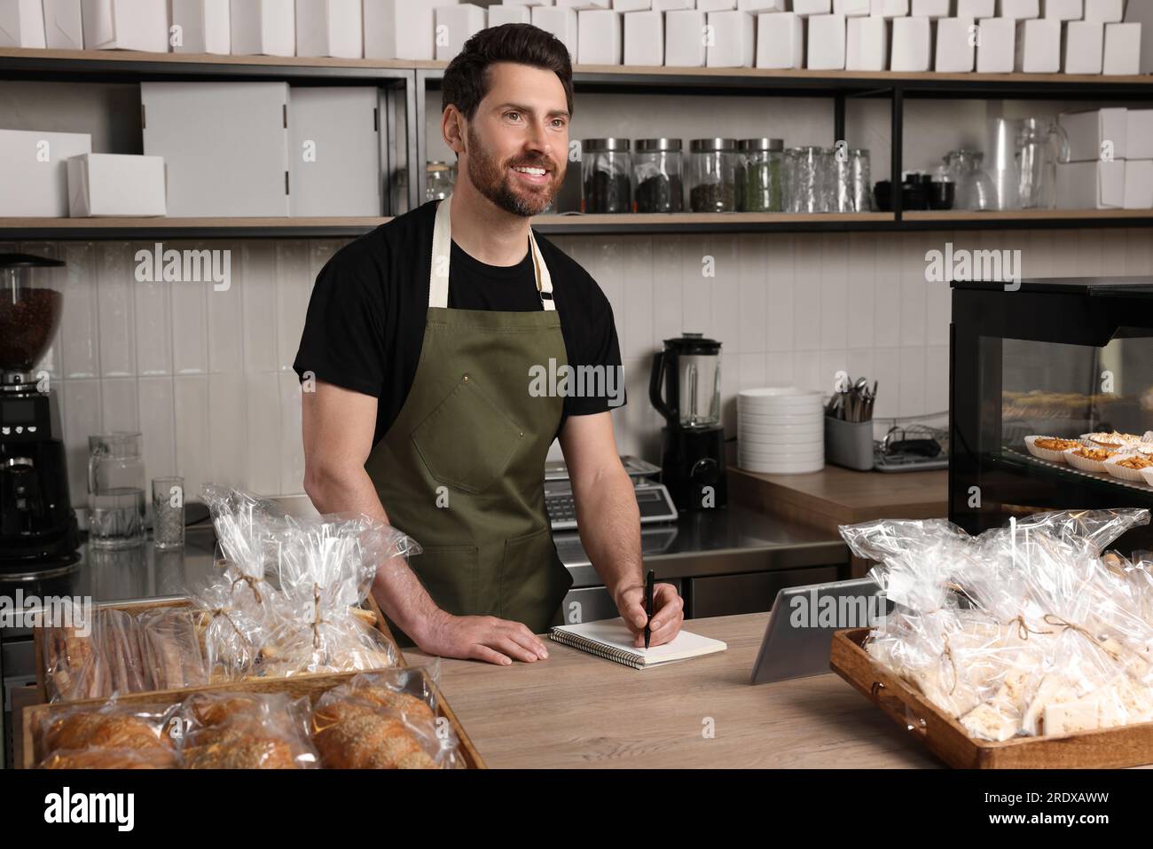 Happy seller writing something at cashier desk in bakery shop Stock ...