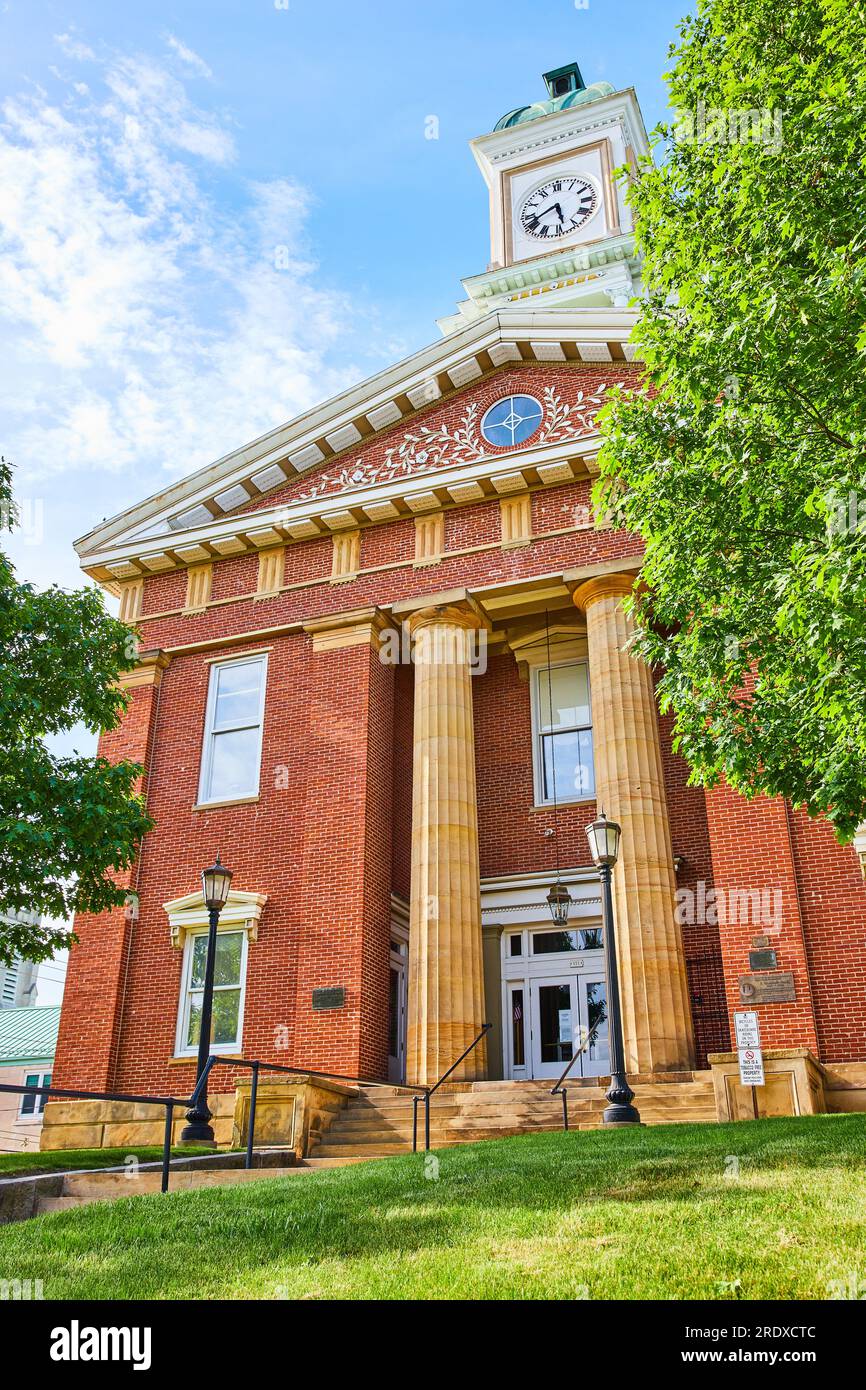 Vertical red brick courthouse with clock tower with blue sky and green ...