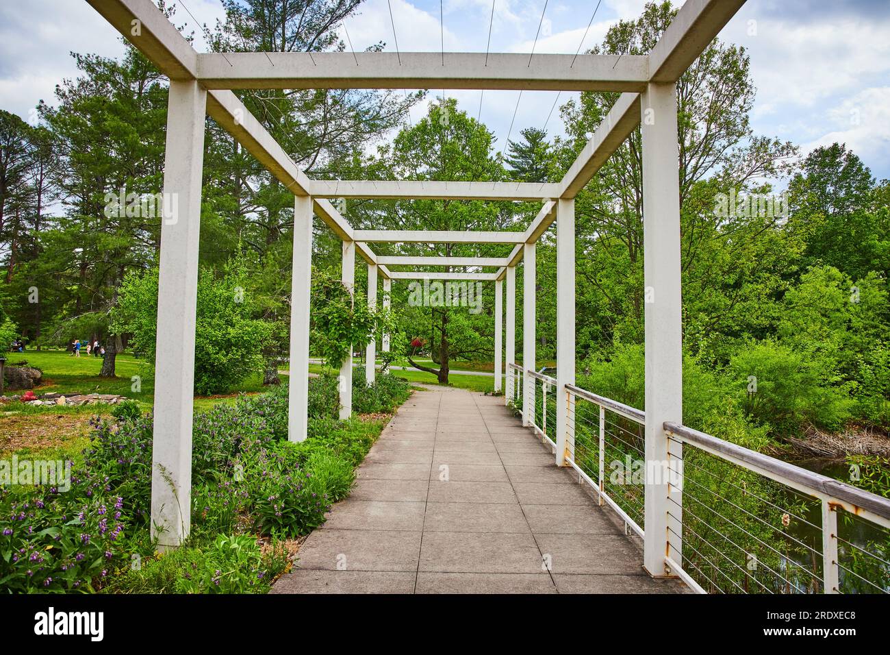 White pergola next to pond with flowers on side of path and park trails ...