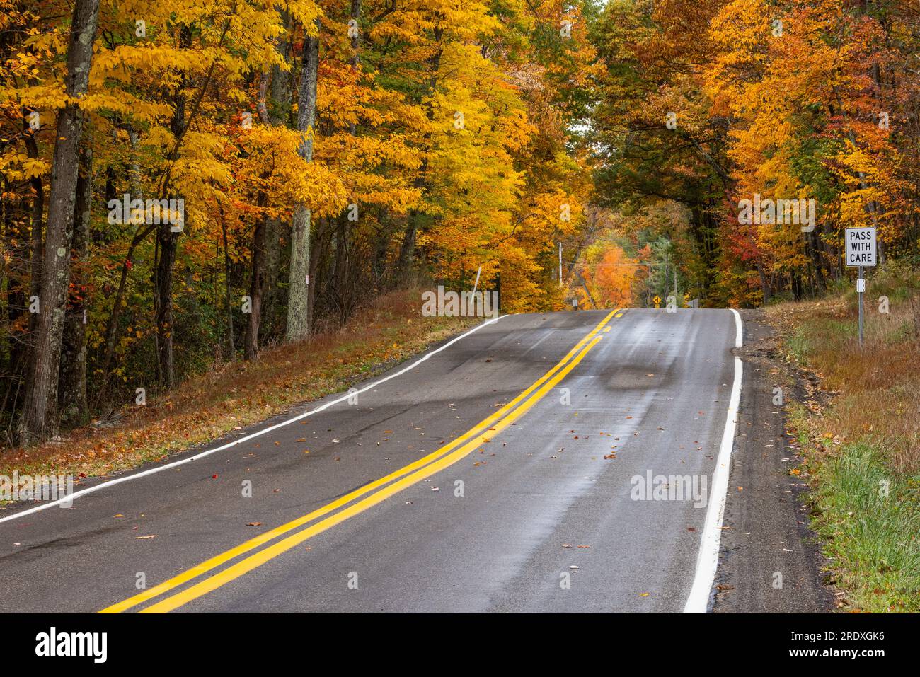 Road leading to crest of a hill with Pass with Care sign in fall ...