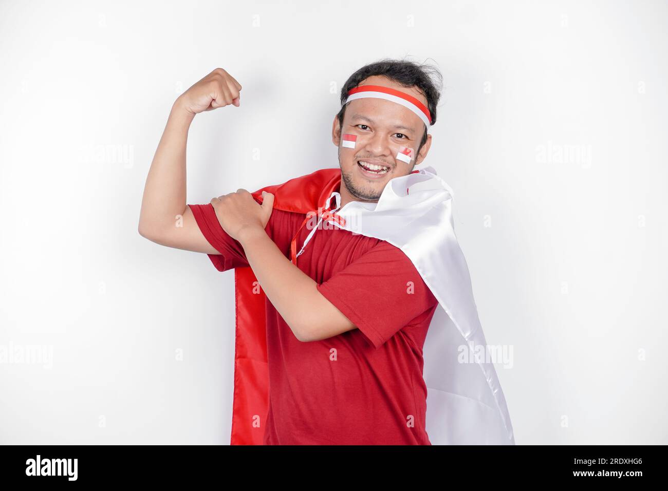 Excited Asian man wearing a red top, flag cape and headband, showing ...
