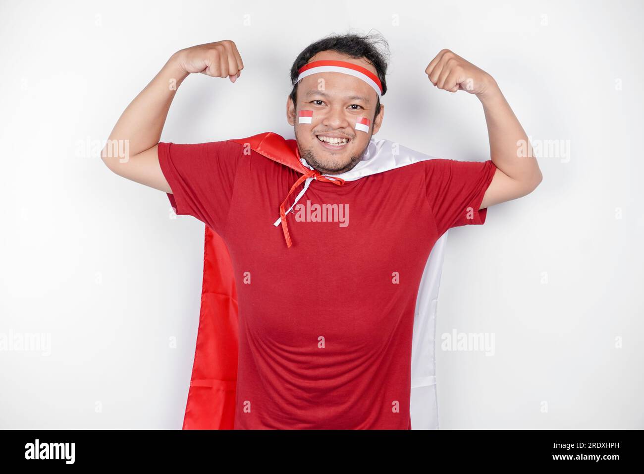 Excited Asian man wearing a red top, flag cape and headband, showing ...