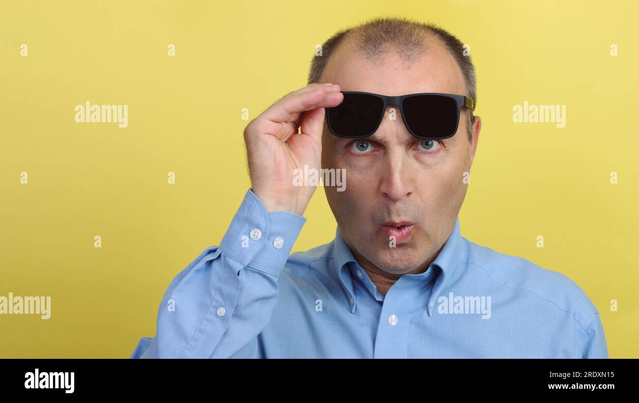 A handsome man 45-55 years old on a yellow background holds glasses in ...