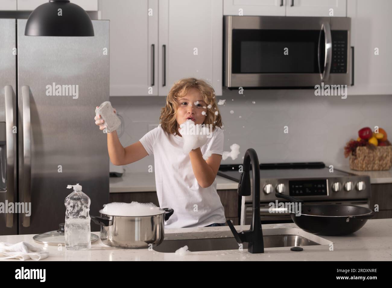 Child boy washing the dishes in the kitchen sink. Dishwashing liquid with a sponge on kitchen ...