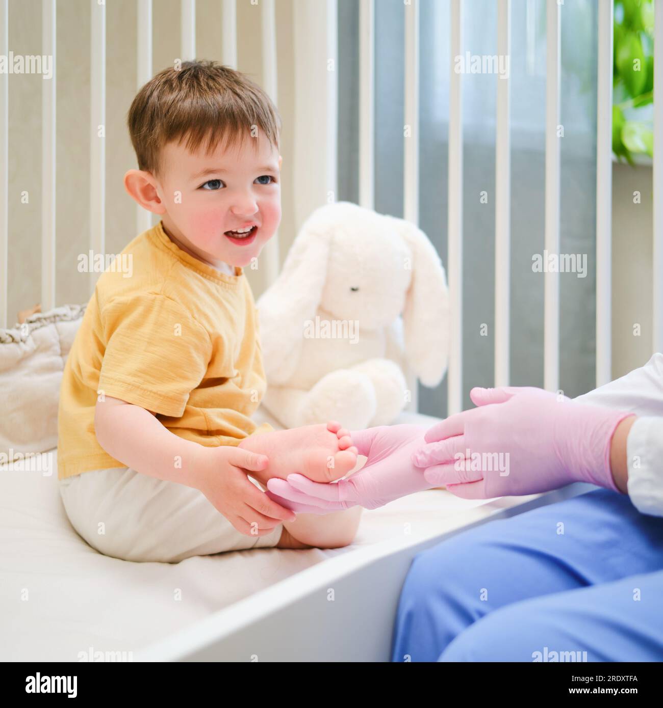 Doctor does gymnastics and foot massage to a toddler baby. Nurse in ...