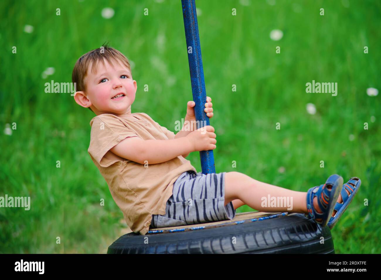 A child is playing on a swing, which is made of a tire of a car wheel ...