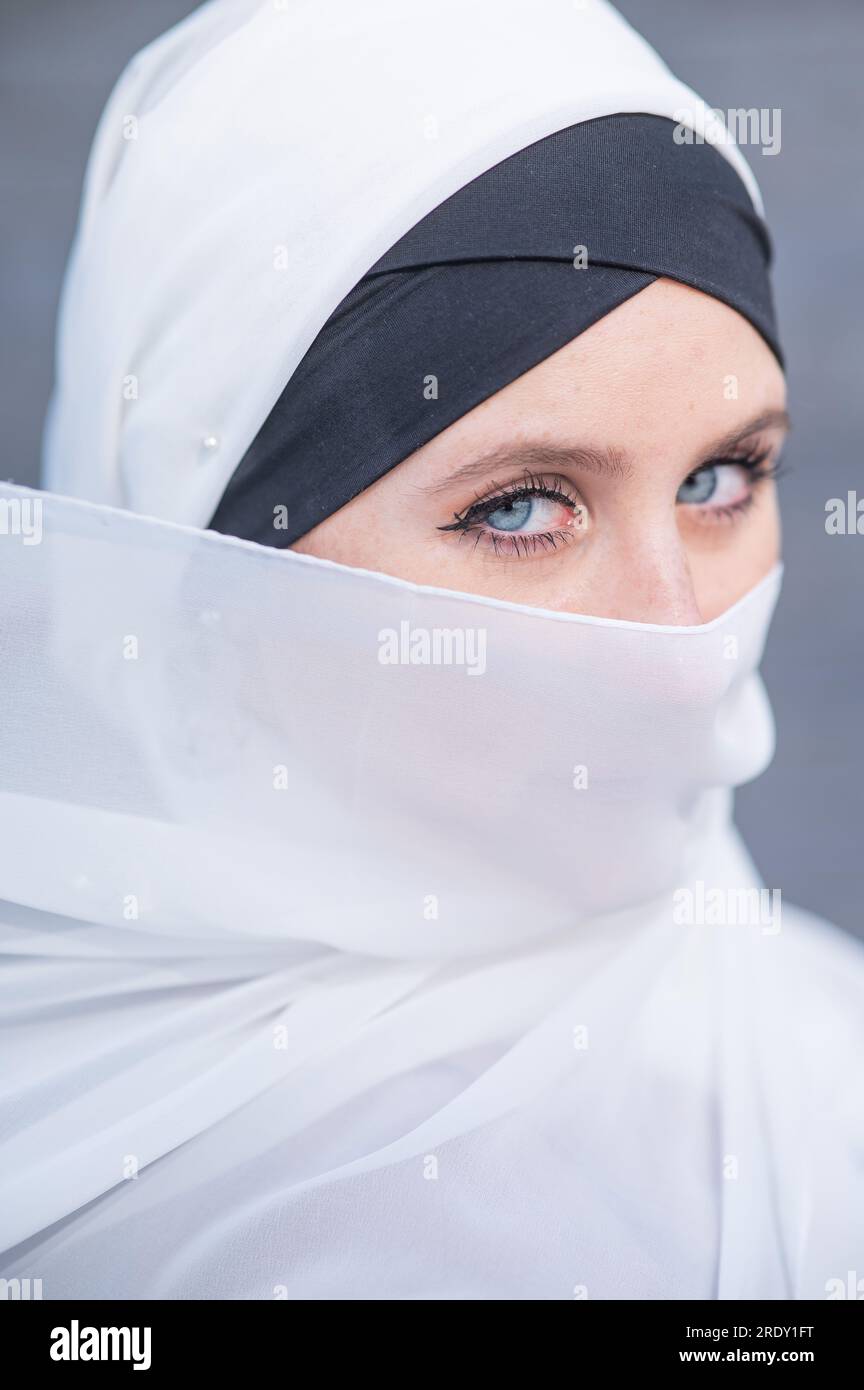 Portrait of a young blue-eyed woman in a hijab against a gray brick ...
