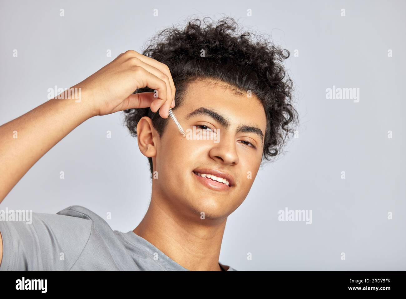 Young handsome smiling guy applying beauty serum on his face to keep ...