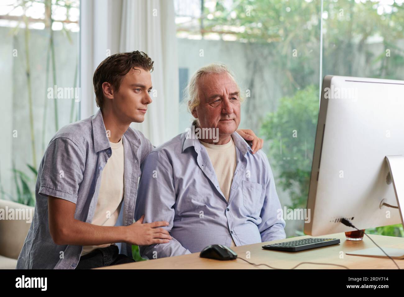 Young man hugging his senior dad when they are video calling family ...