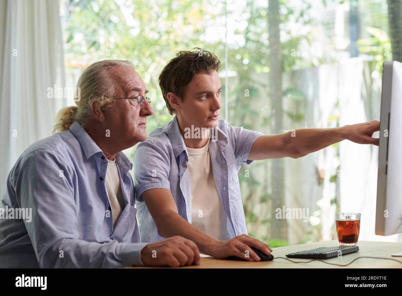 Teenage boy pointing at laptop screen when explaining grandfather how ...