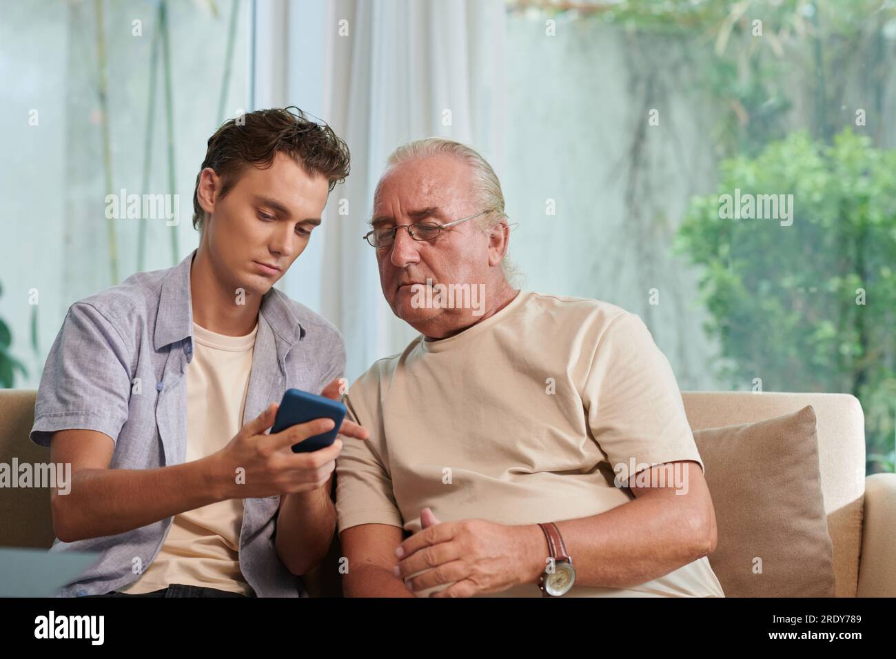 Young man showing senior man how to send text messages, voice messages ...