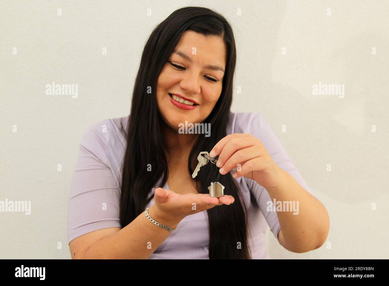 Latin adult woman shows the keys to her new home on a house-shaped ...