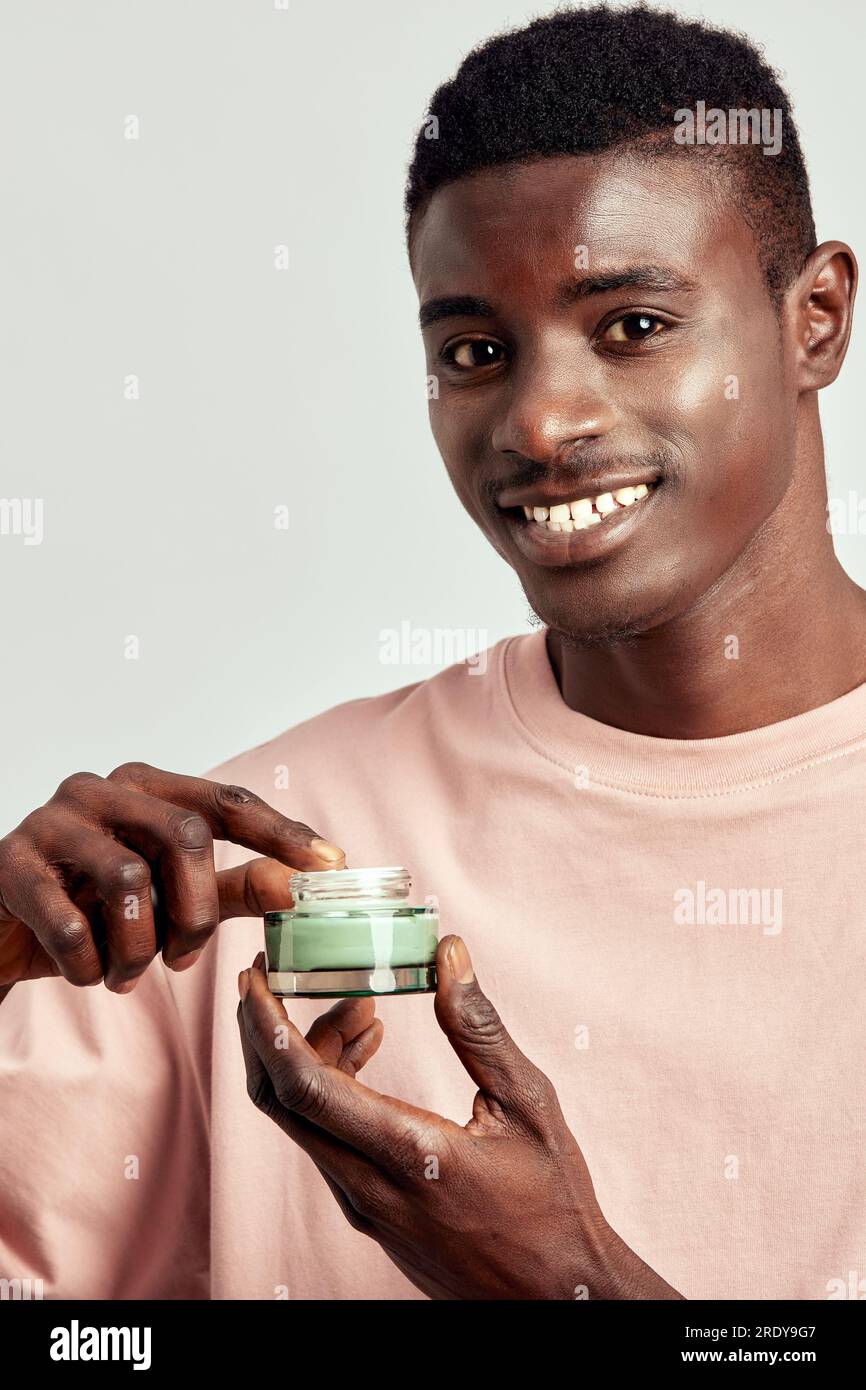 Young handsome black guy applying moisturizing skin balm from a small ...