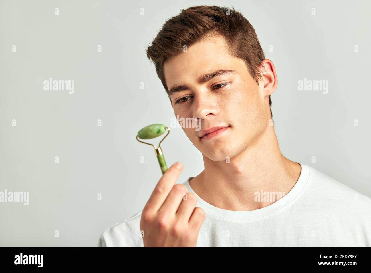 Young handsome smiling brown haired guy using jade de-puffing face ...