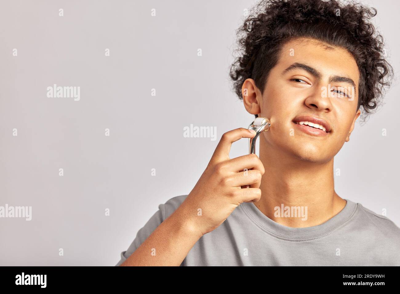 Young handsome smiling guy using de-puffing face roller to keep his ...
